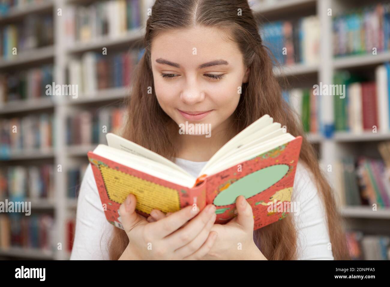 Close up of a charming teen girl smiling, reading a book at local ...