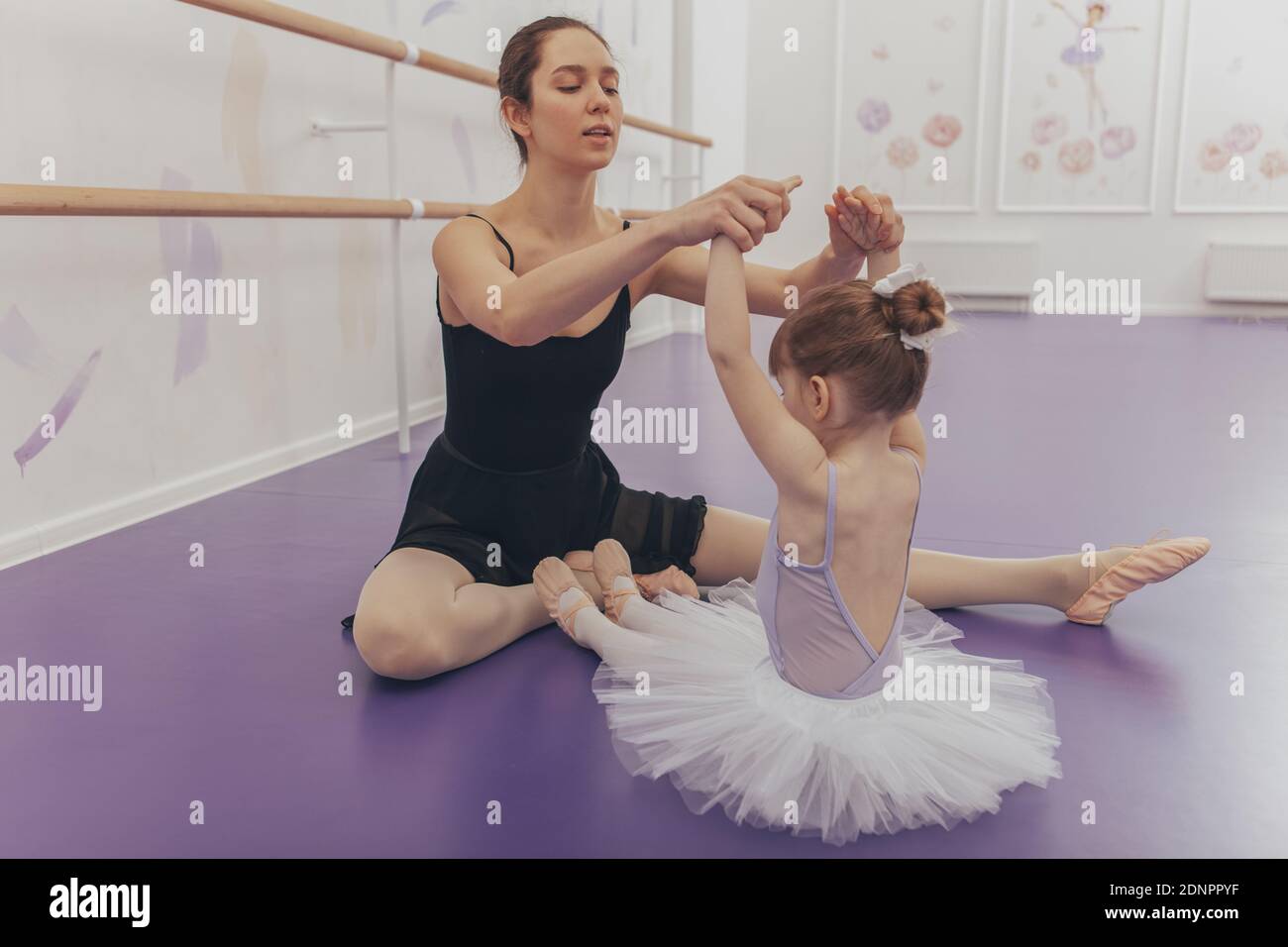 Adorable little ballerina exercising with her ballet teacher at dance ...