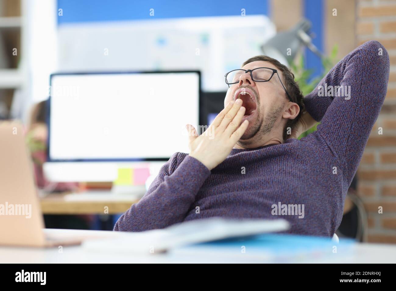 Young man siting at table in office and yawning Stock Photo - Alamy
