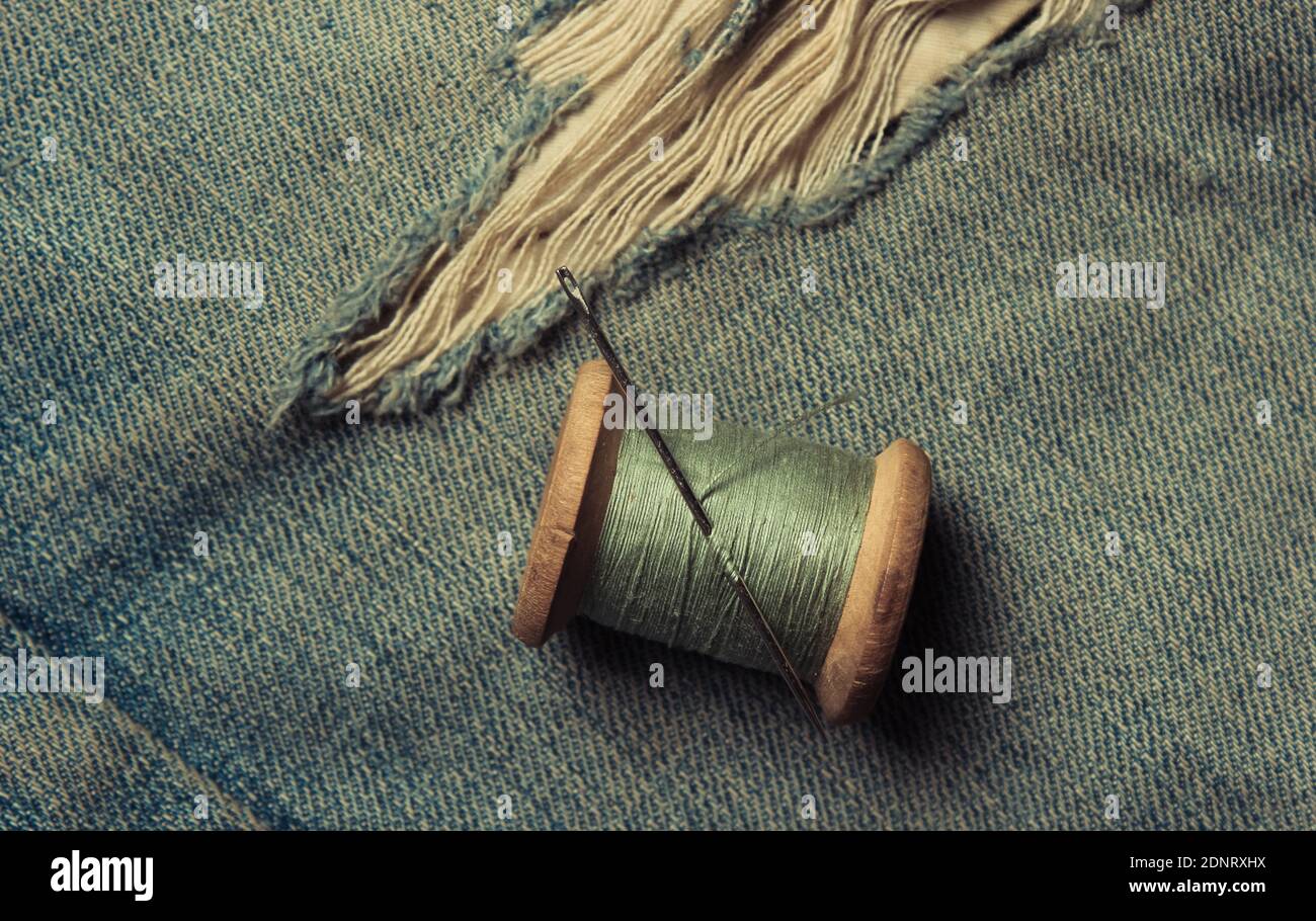 Retro skein thread with a needle on torn, rubbed jeans, sewing jeans ...