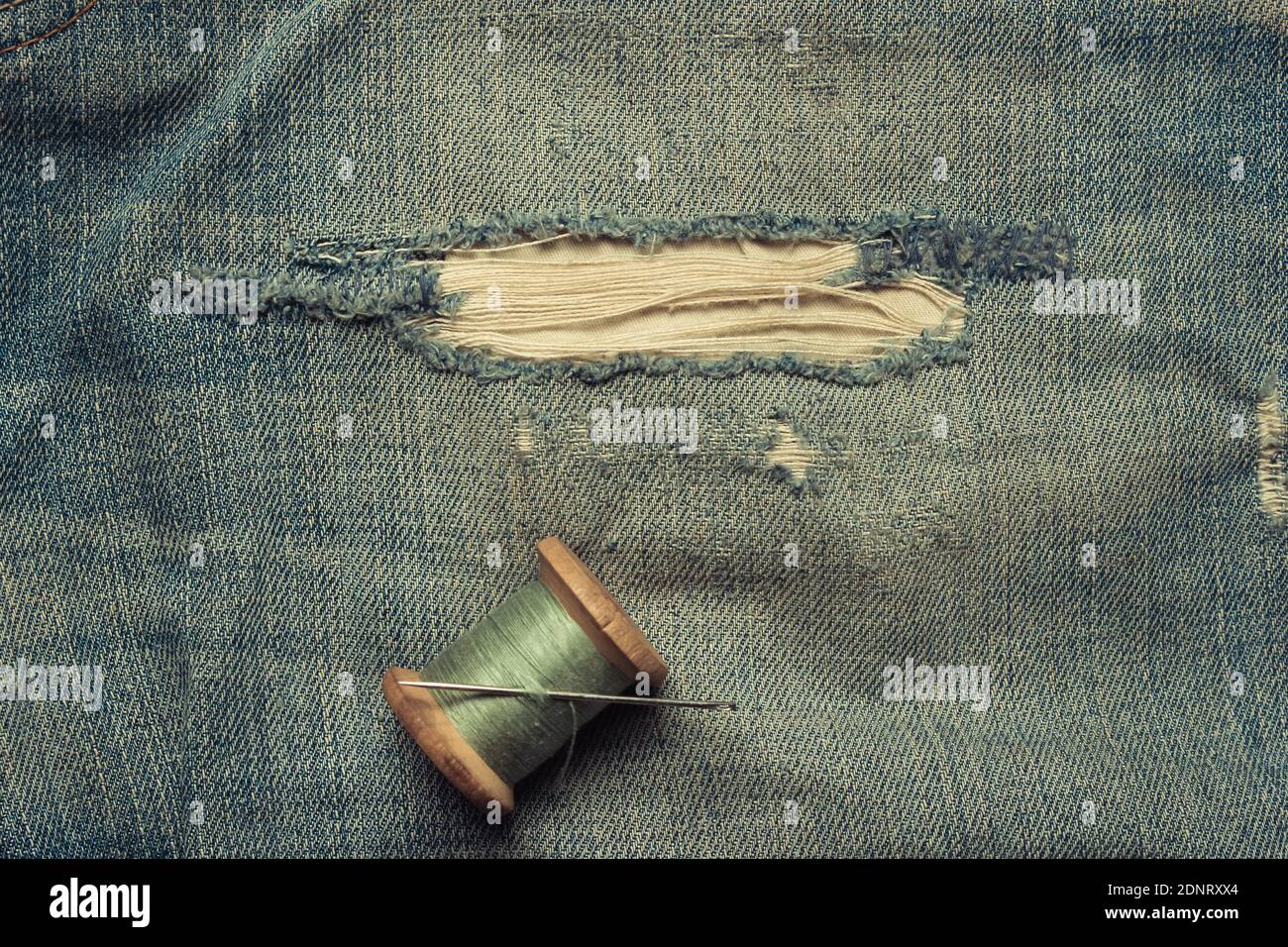 Retro skein thread with a needle on torn, rubbed jeans, sewing jeans ...