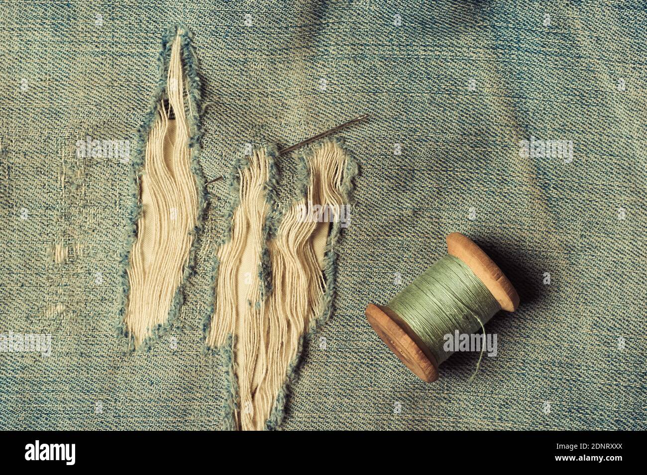 Retro skein thread with a needle on torn, rubbed jeans, sewing jeans ...