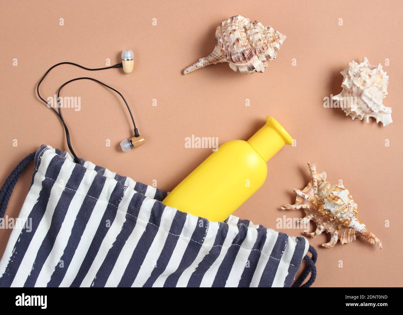 Beach bag, seashells, earphones, bottle of suntan cream on a brown ...