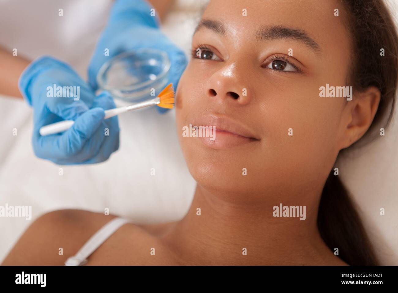 Close up of a gorgeous African woman smiling while beautician applying ...