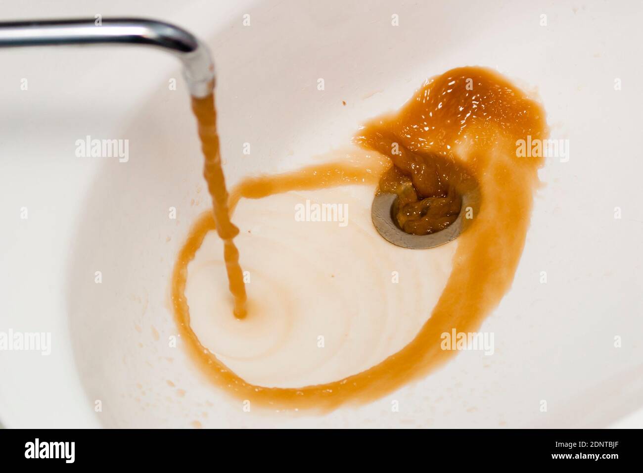 Dirty water from the tap. Rusty water flows into a white sink from a ...