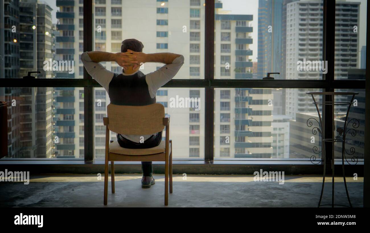 Rear View Of Man With Hands Behind Head Sitting Against Window Stock ...