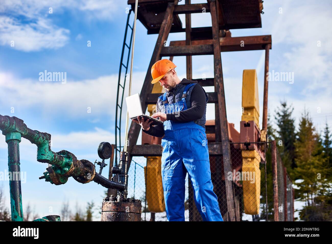 Engineer in work overalls and helmet checking oil pumping unit at oil ...