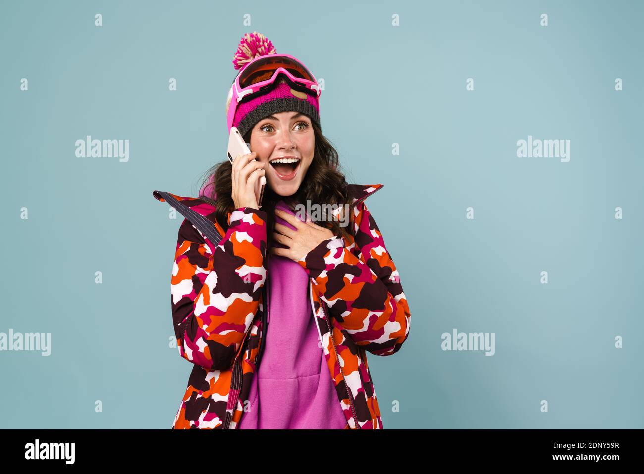 Cheerful young woman wearing winter jacket using mobile phone isolated ...