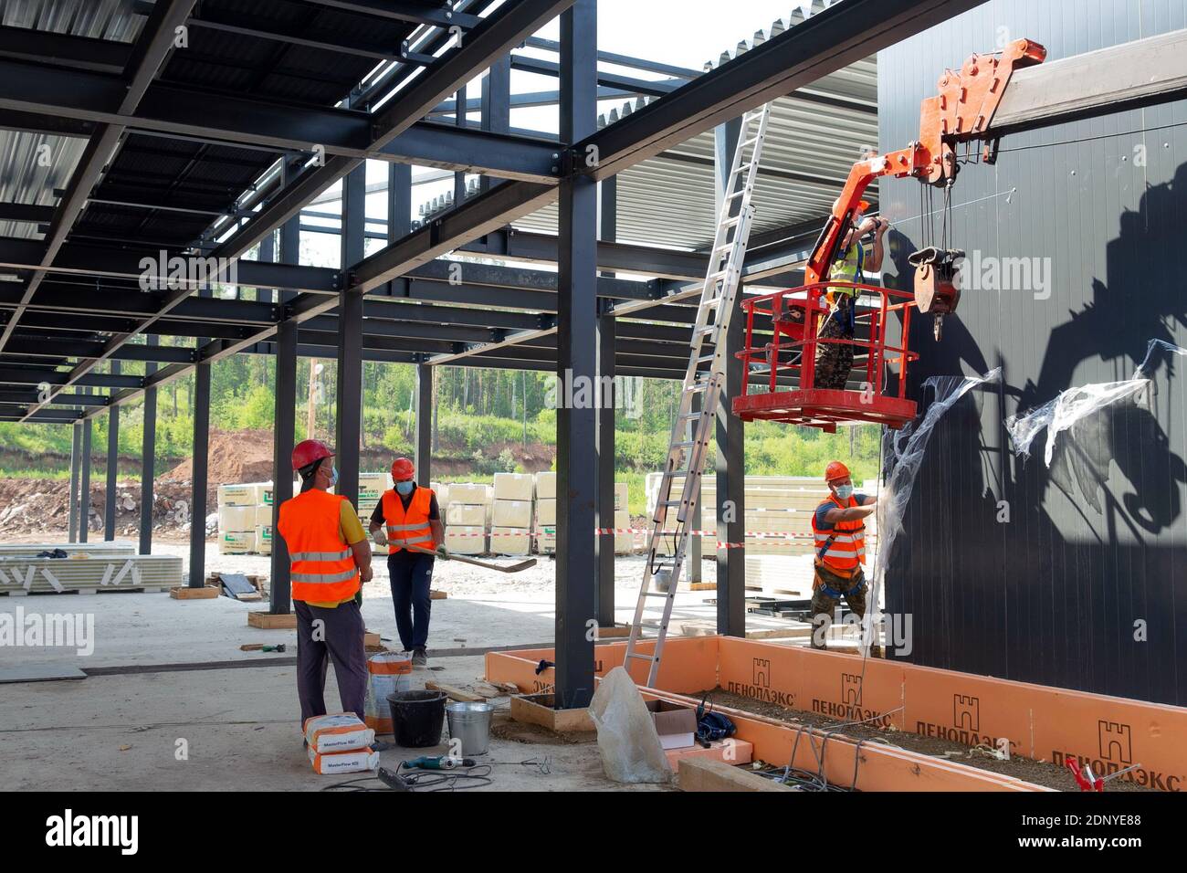 An installer in a hanging cradle and a work team are installing wall ...