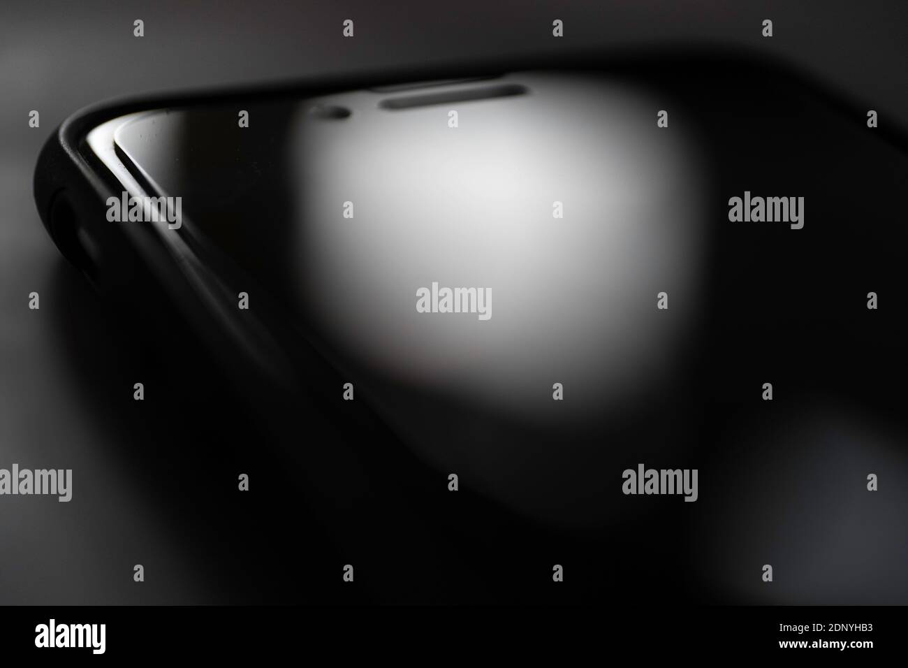 Shiny black screen of a black cell phone lying on a dark table ...