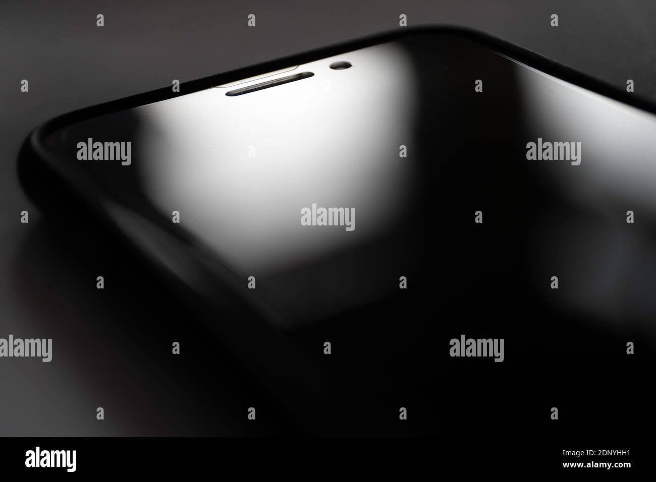 Gaze at the shiny black screen of a black smartphone lying on a dark ...