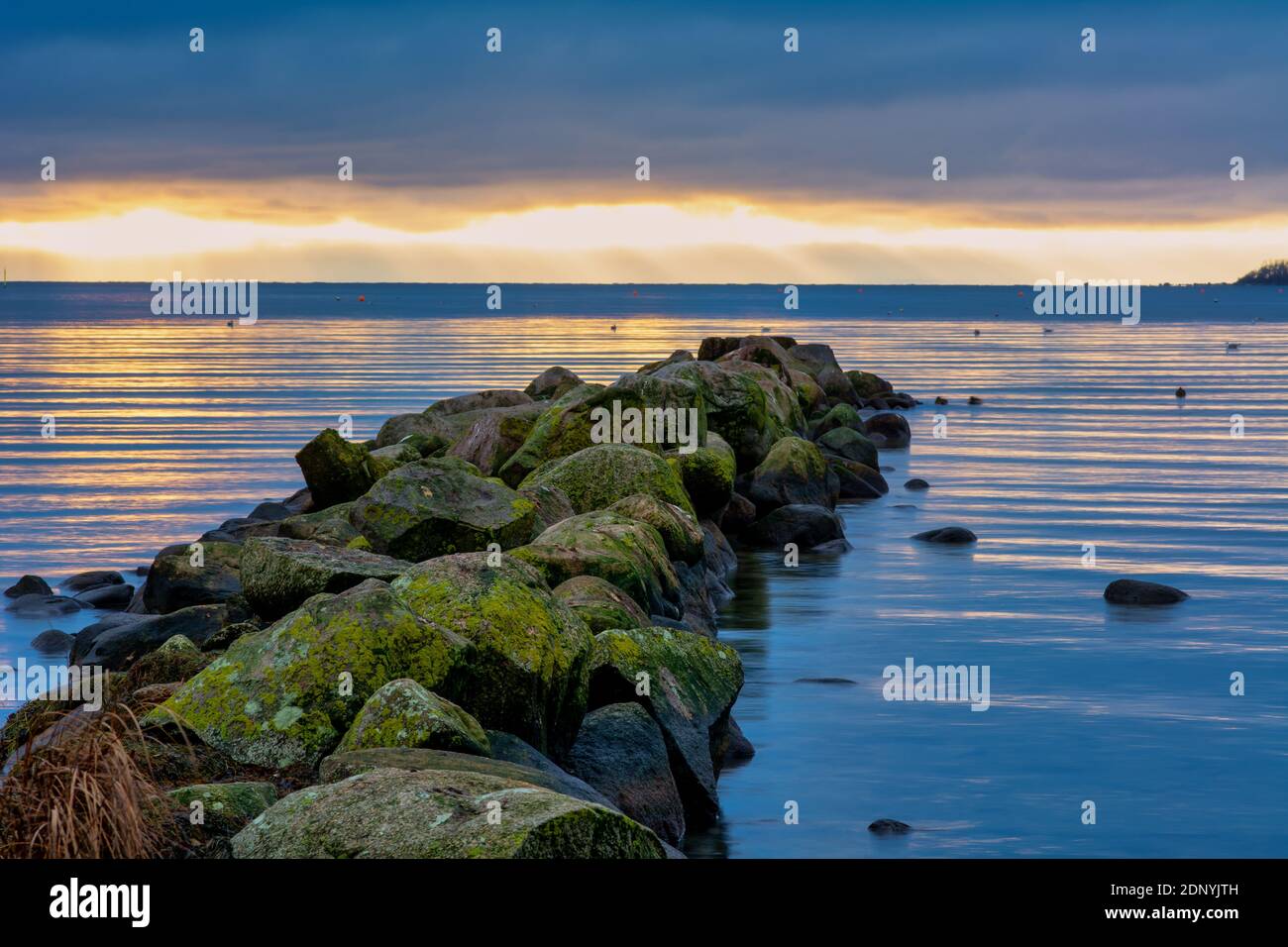 A beautiful sunset over the green boulders on a wave breaker. Photo ...