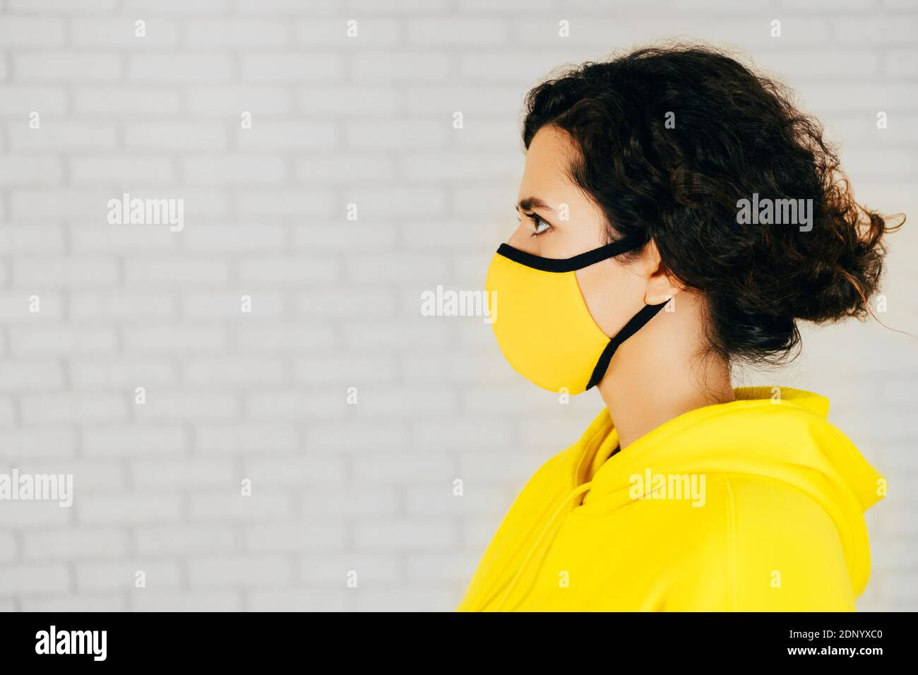 Profile of brunette in vibrant yellow hoodie and fabric mask standing ...