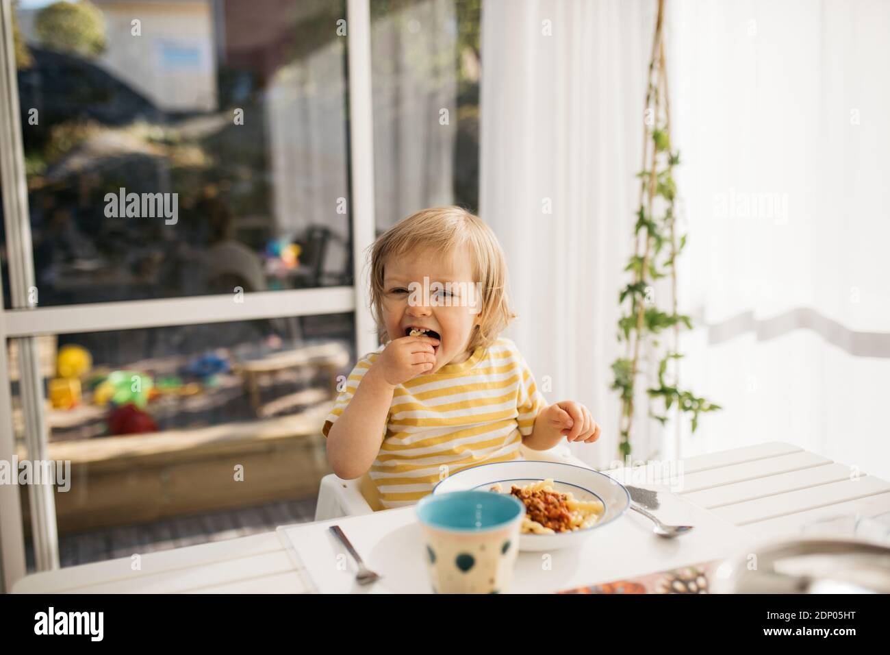Toddler girl eating at table Stock Photo - Alamy