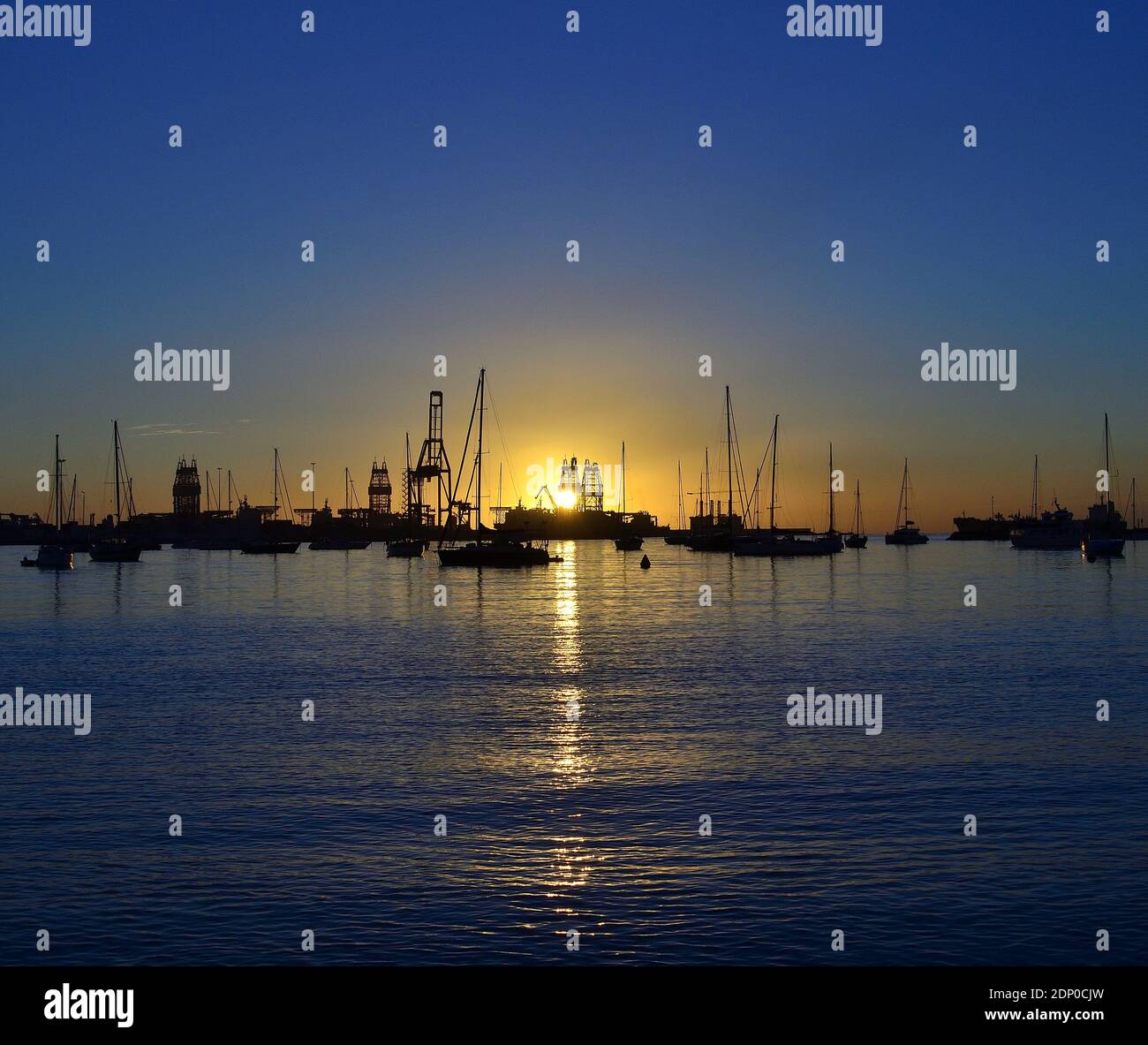 Sunrise in the bay with calm sea, intense blue sky and backlit port ...