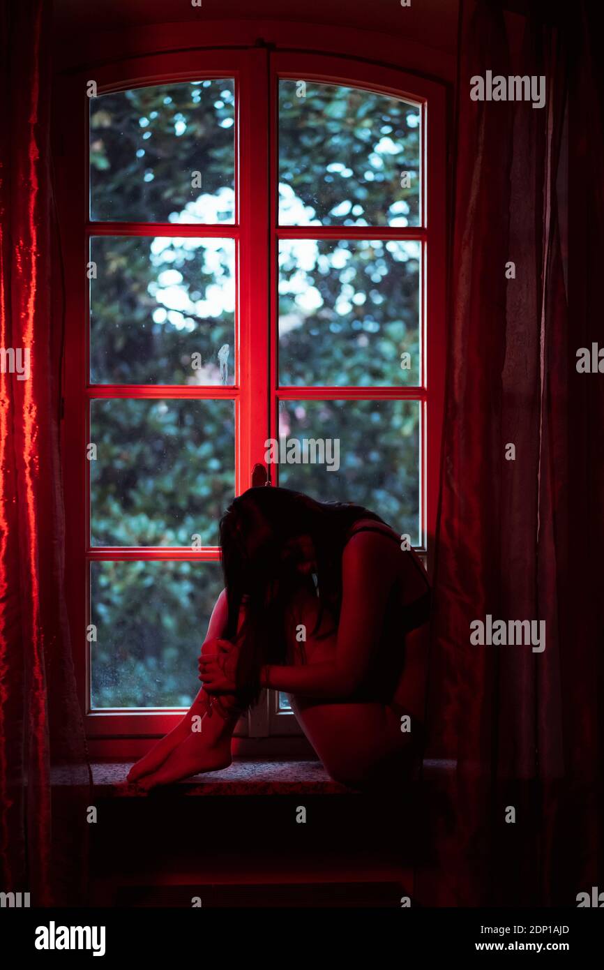 Woman sitting with hugging knees at window sill Stock Photo - Alamy