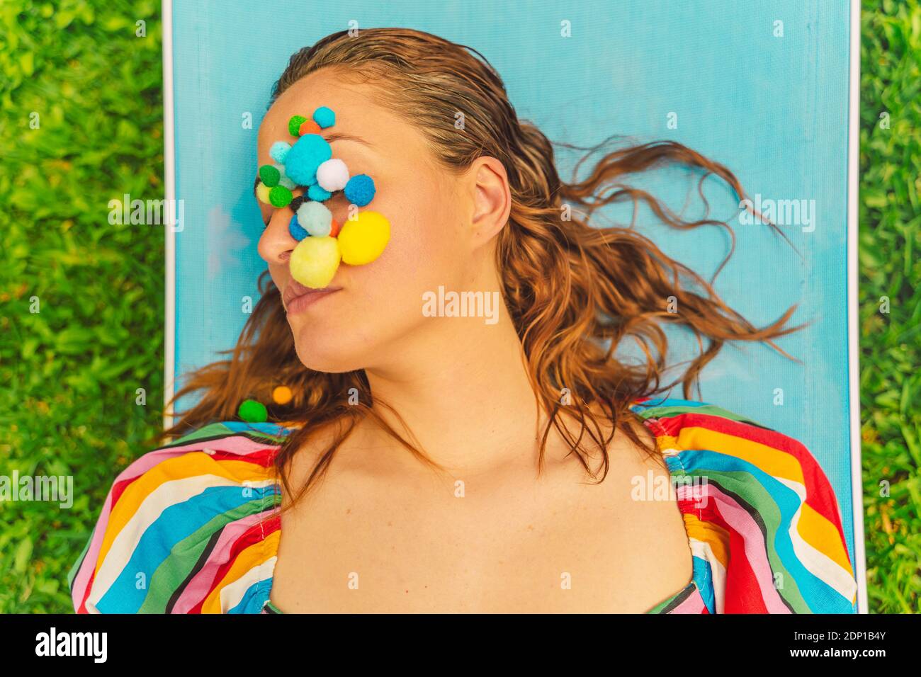 Portrait of woman with colourful pom poms on her face relaxing on sun ...