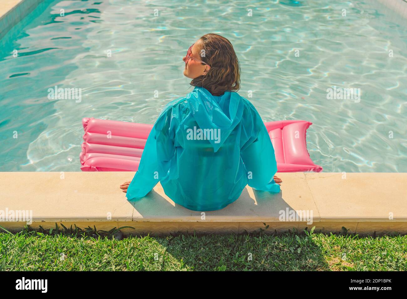 Back view of woman in blue rain coat sitting at poolside Stock Photo ...
