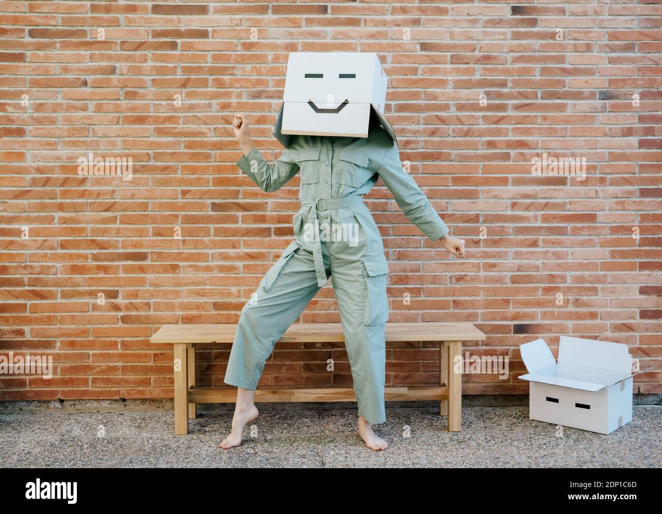 Woman wearing cardboard box with happy face, dancing in front of bench ...
