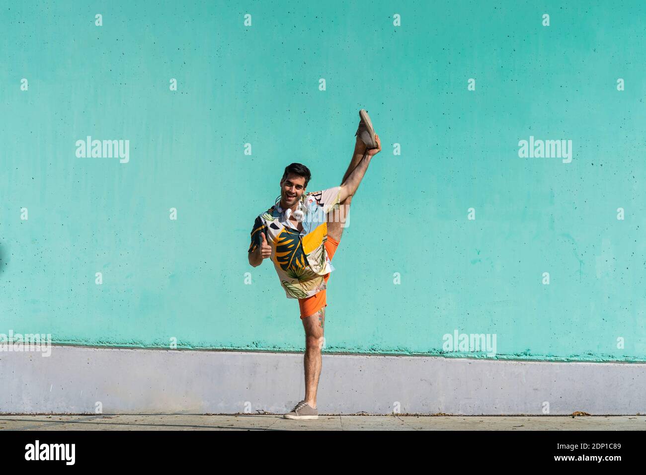 Casual man doing standing splits in front of green wall Stock Photo - Alamy