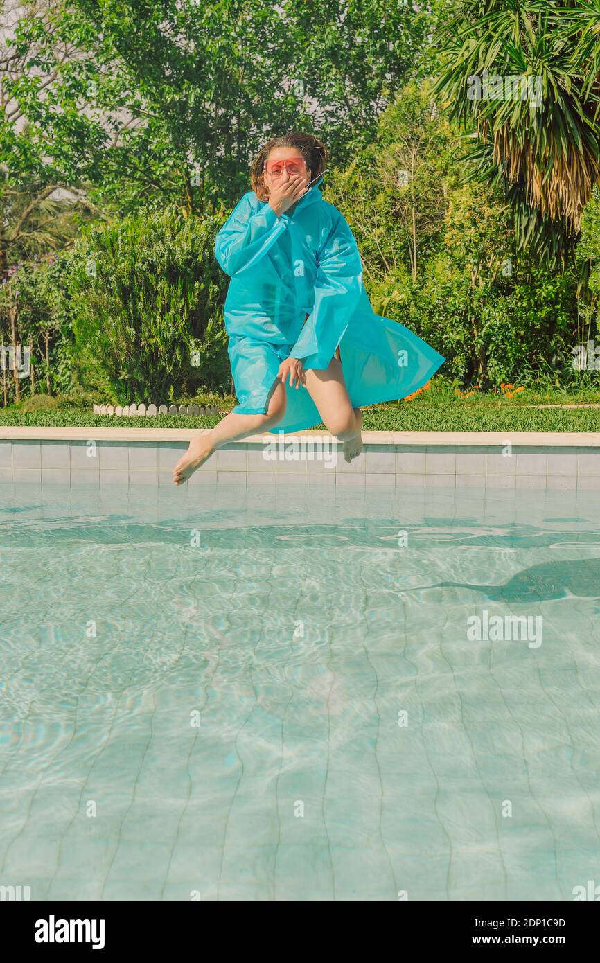 Woman in blue rain coat jumping into swimming pool Stock Photo - Alamy