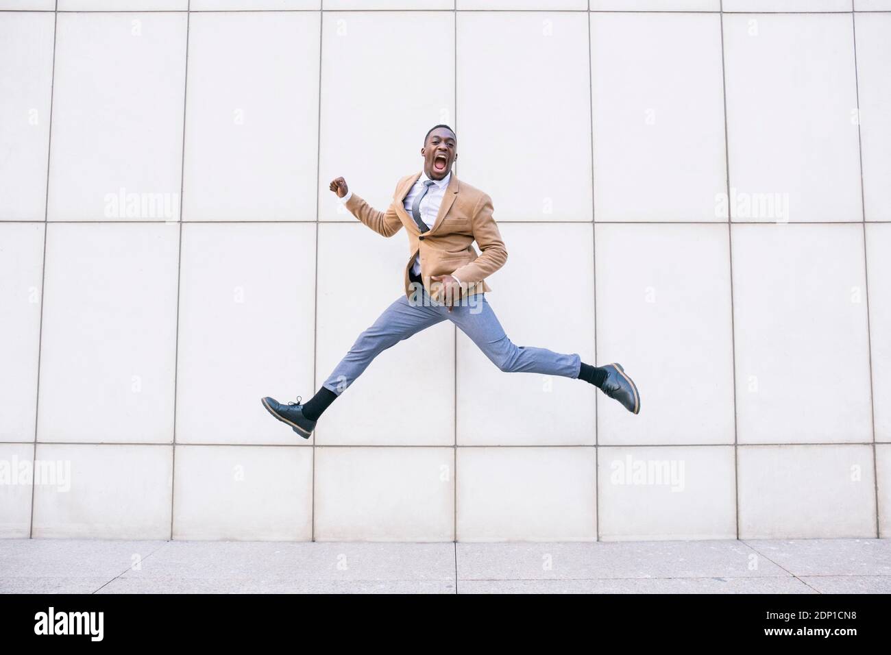 Young businessman jumping and shouting in front of a wall Stock Photo ...