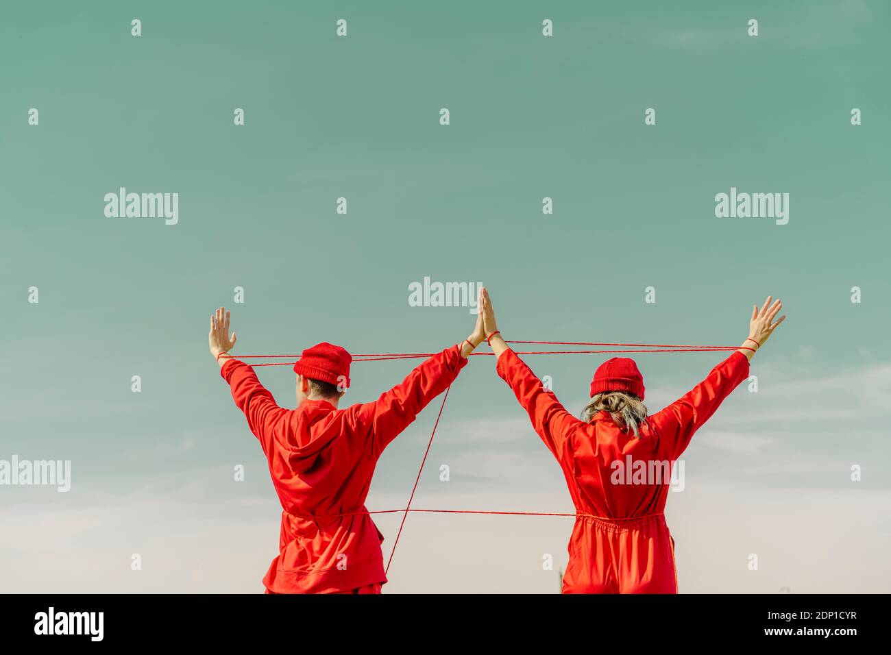 Back view of young couple wearing red overalls and hats performing with ...