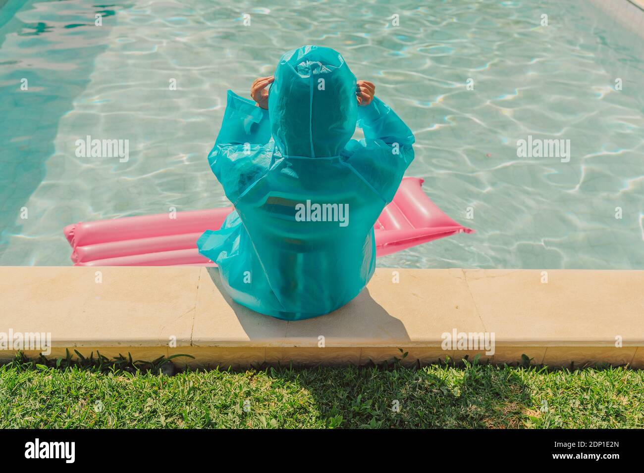 Back view of woman wearing blue rain coat sitting at poolside Stock ...