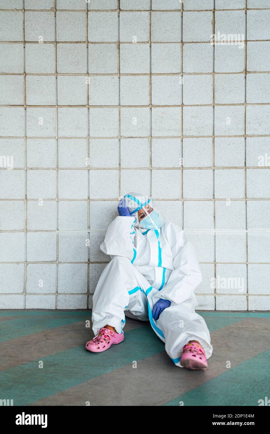 Contemplating female nurse with head in hands sitting against tiled ...