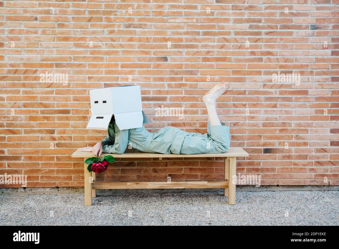 Bored woman with red rose, wearing cardboard box with sad face, lying ...