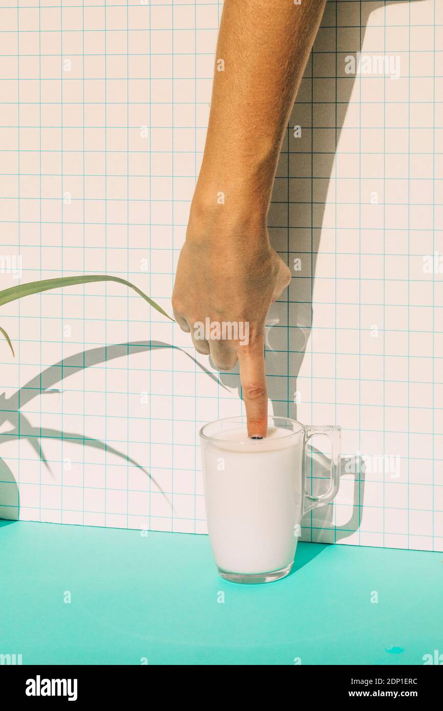 Female putting finger in milk cup on blue table Stock Photo - Alamy