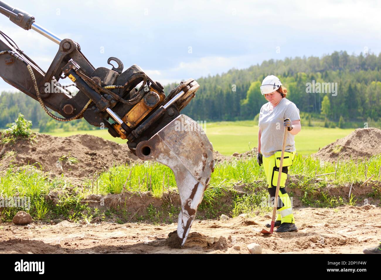 Female worker standing near digger scoop Stock Photo - Alamy
