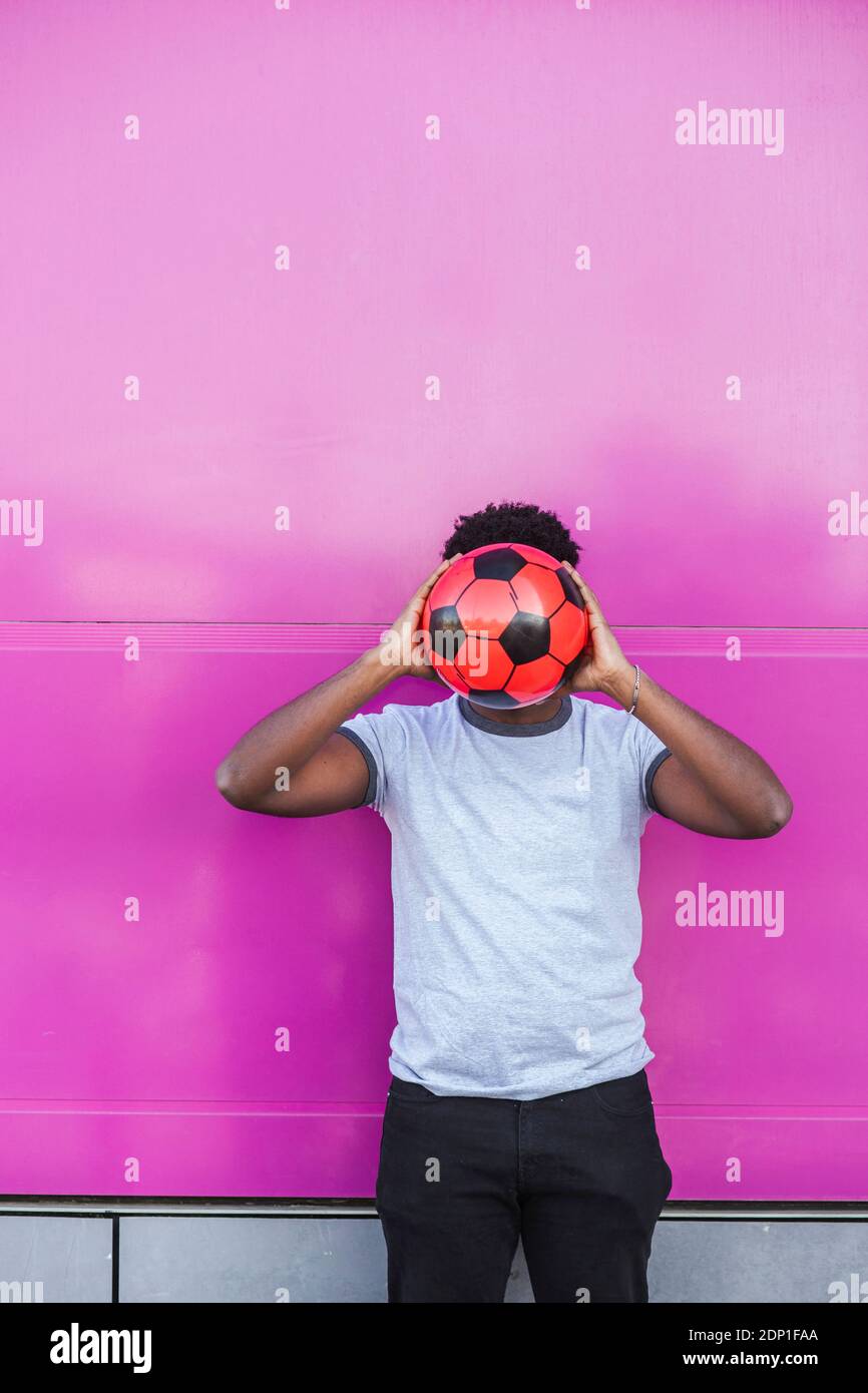 Young man holding soccer ball in front of face while standing against ...