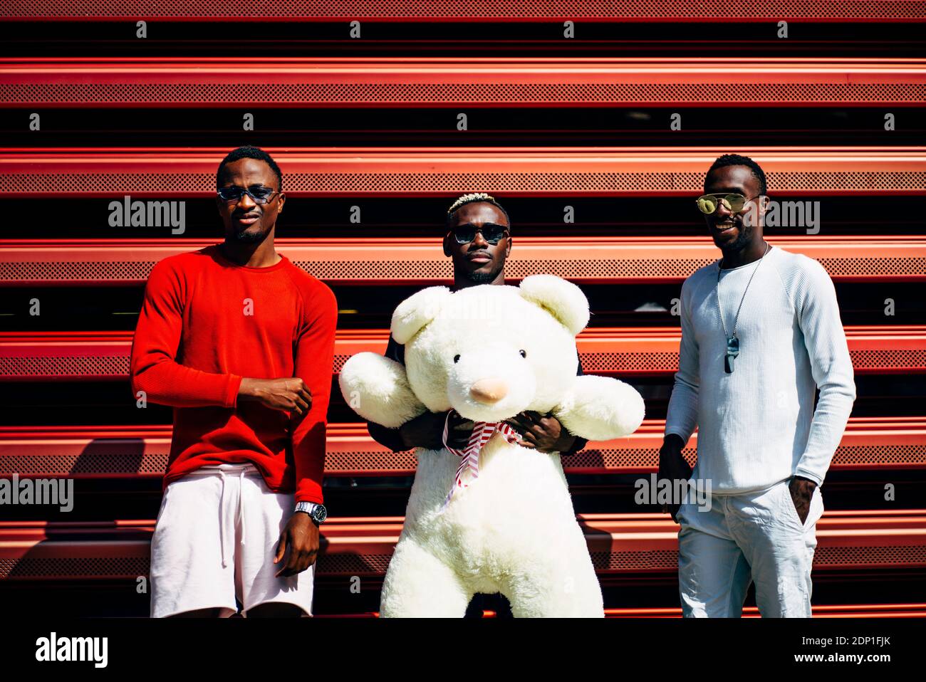 Portrait of three cool young men with huge teddy bear at red wall Stock ...