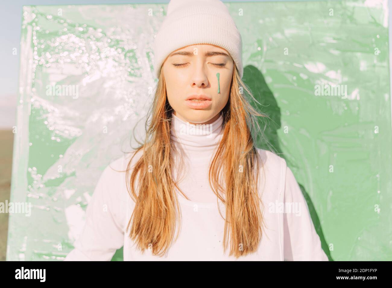 Young woman standing in front of green canvas with green tear on her ...