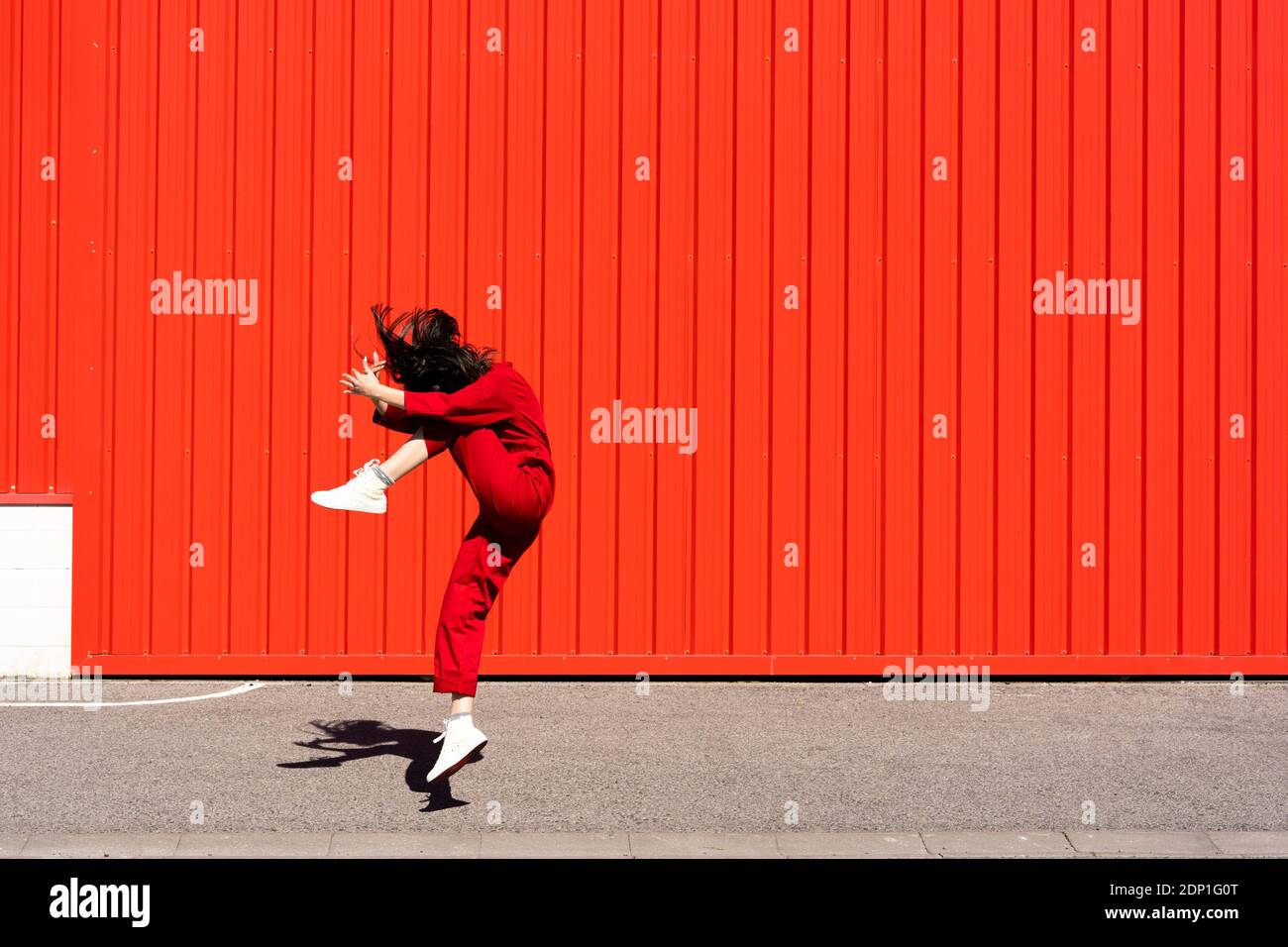 Woman dressed in red overall jumping in the air in front of red roller ...