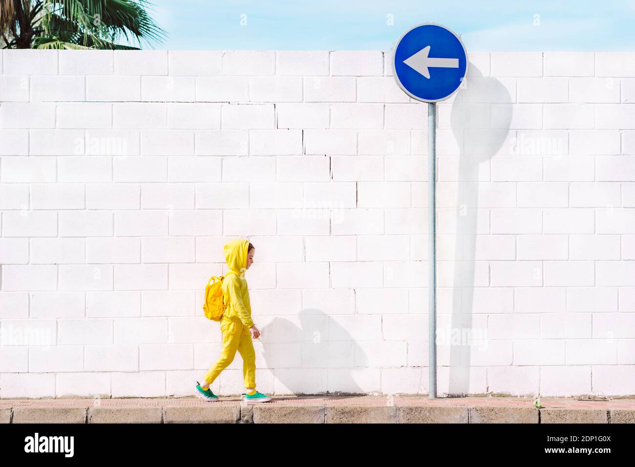 Girl walking at a traffic sign, direction left, in front of a white ...