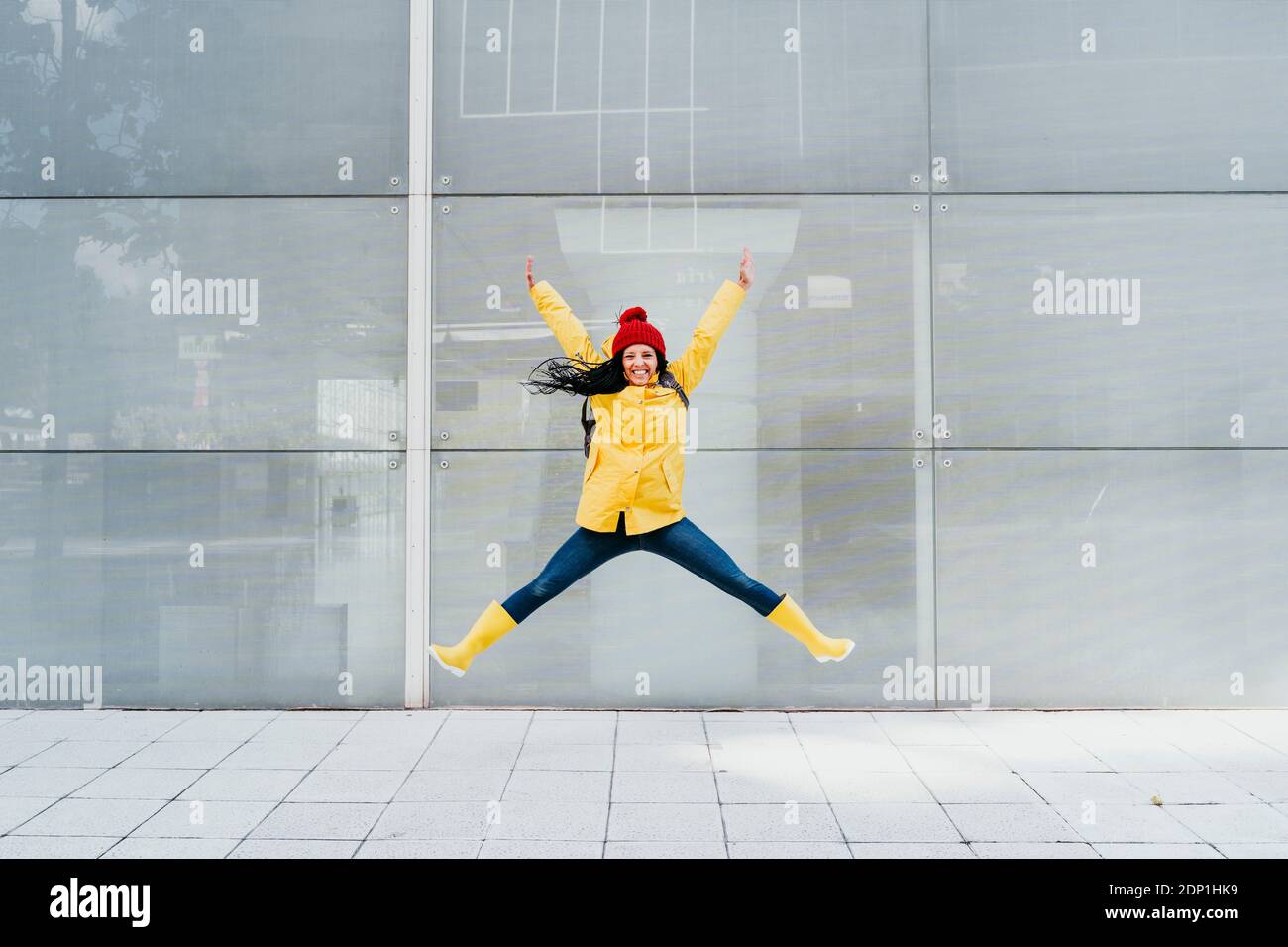 Smiling woman jumping with hand raised on footpath against building ...