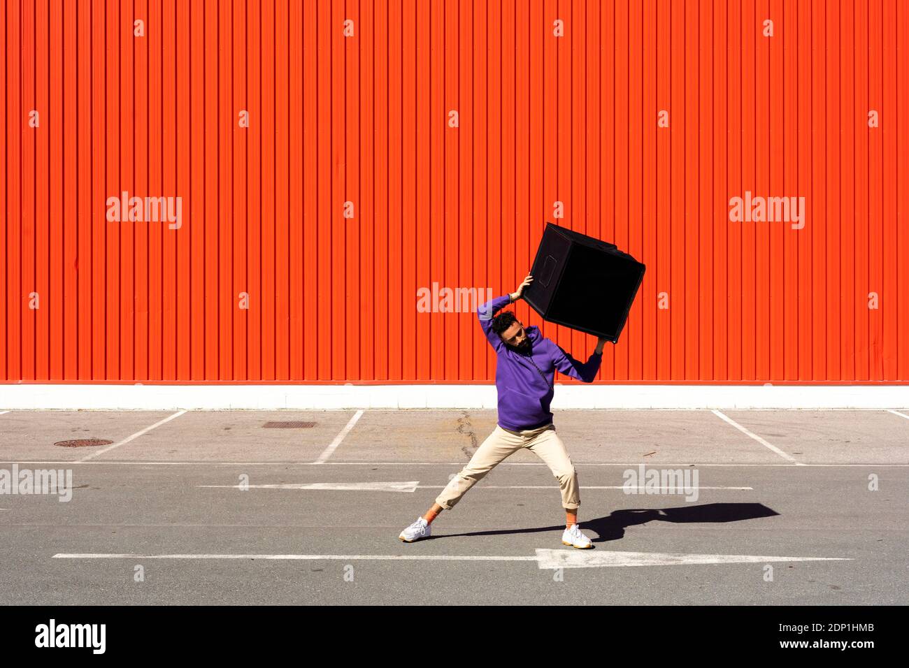 Young man carrying a box in front of a red wall Stock Photo - Alamy
