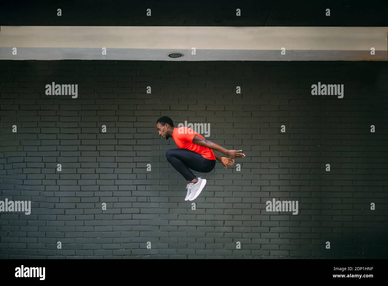Young sportive man jumping in front of a brick wall Stock Photo - Alamy