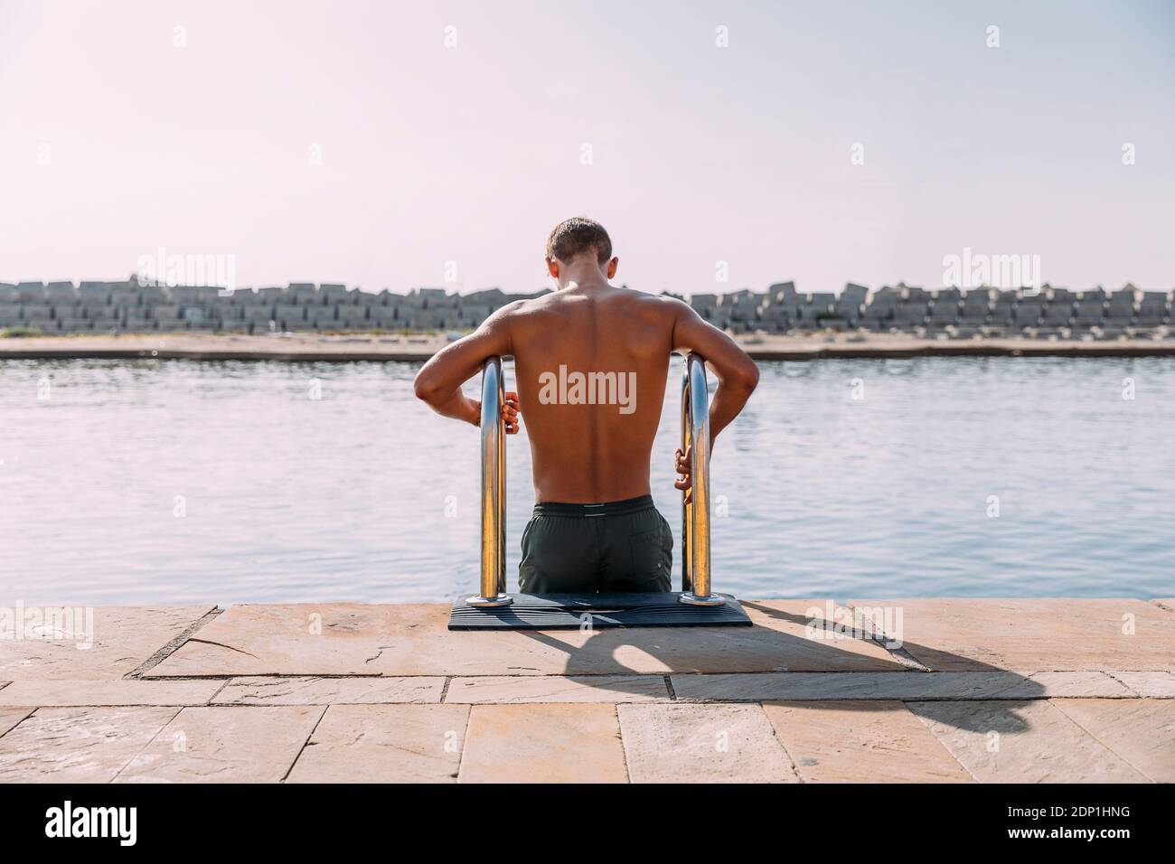 Young man getting into the water from jetty Stock Photo - Alamy