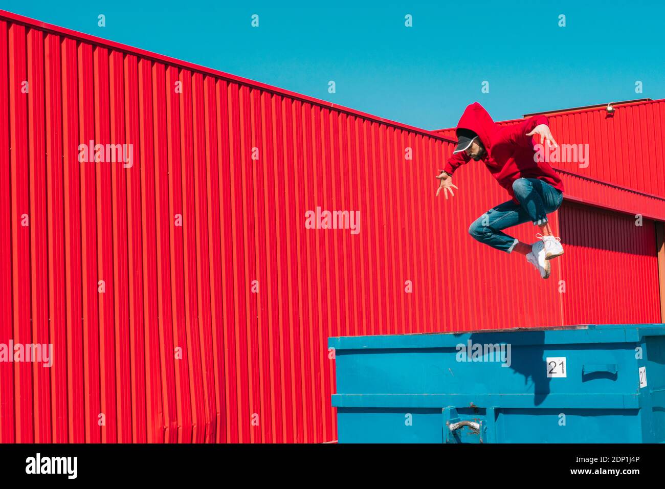Young man wearing red hooded jacket jumping from edge of container in ...