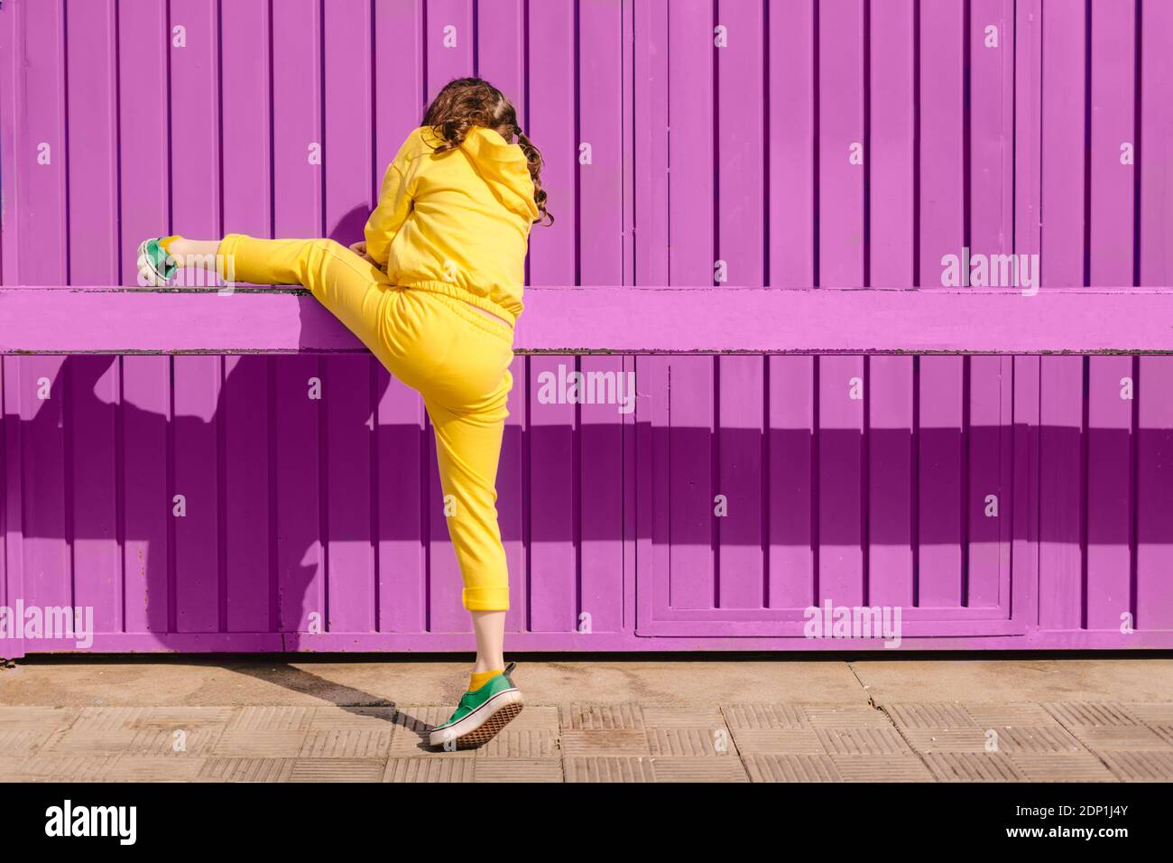 Back view of girl dressed in yellow climbing on bar in front of purple ...