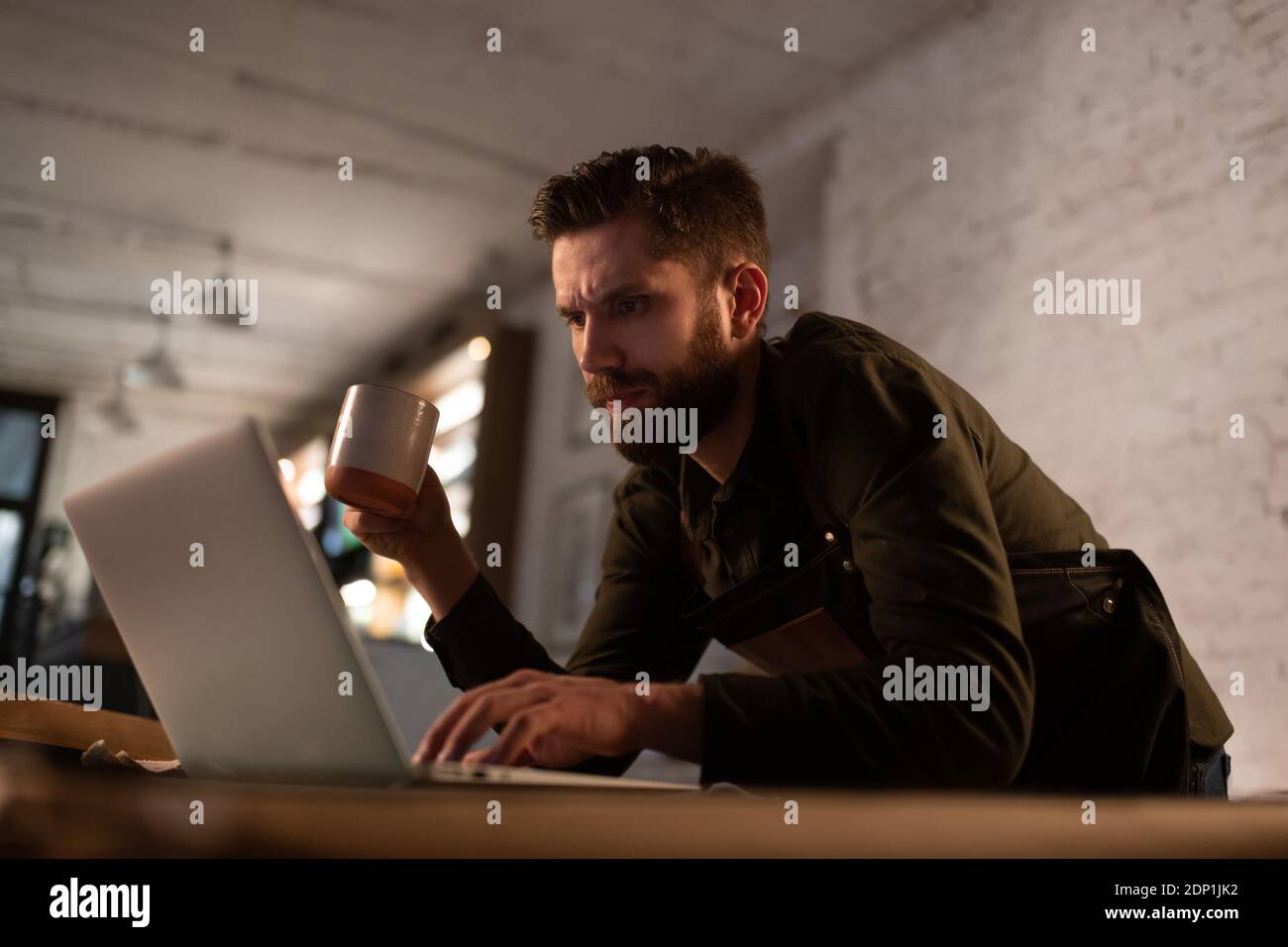 Low angle of bearded male artisan with mug of hot beverage frowning and ...