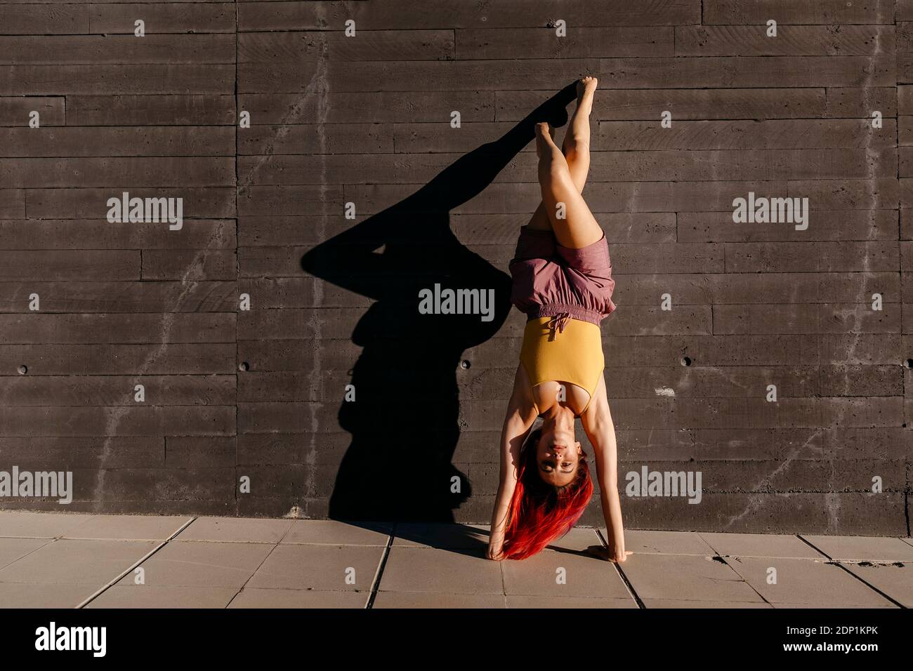 Woman doing a handstand barefoot with black urban wall background in ...