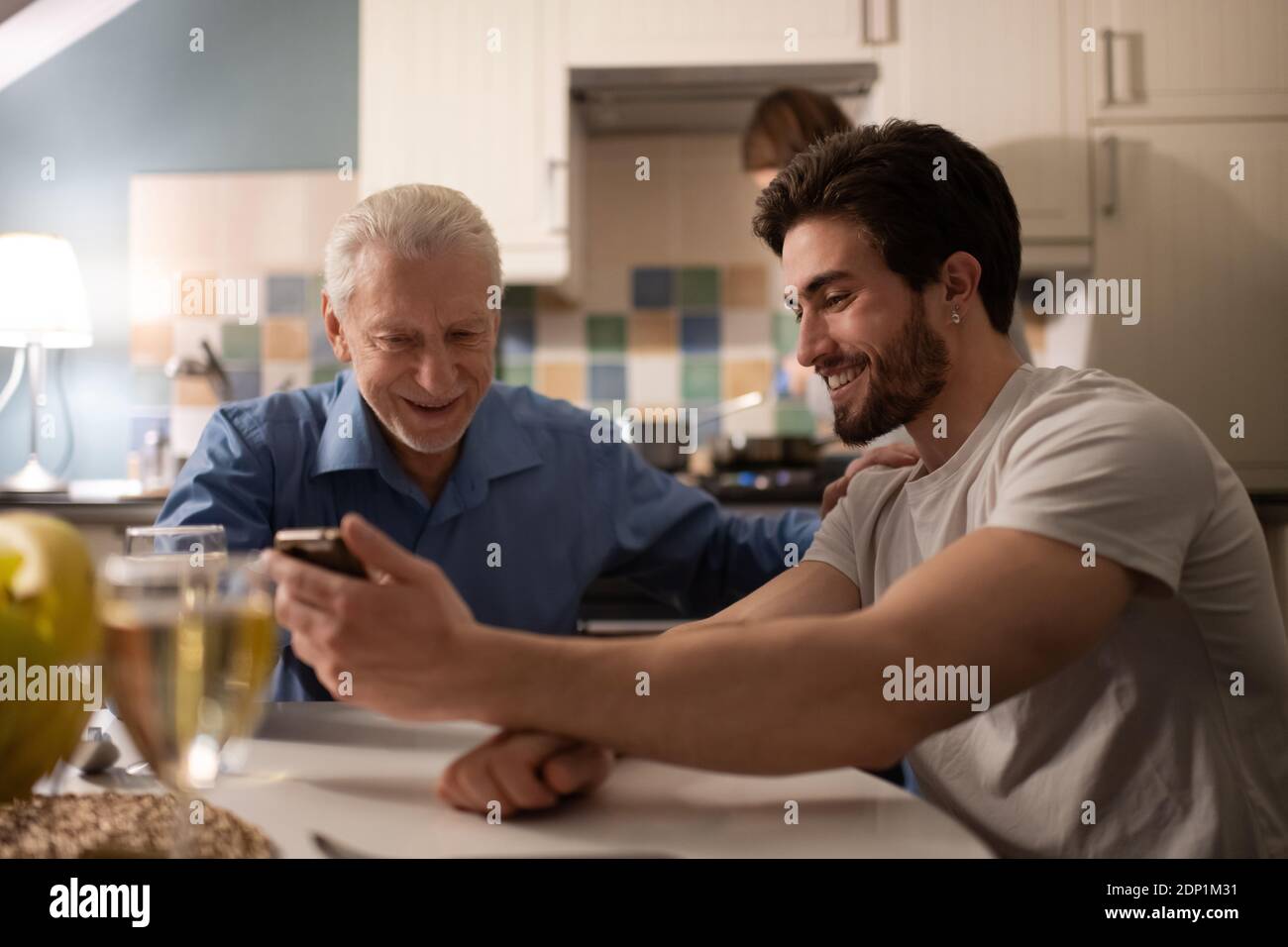 Cheerful elderly man supporting bearded son showing photos on ...