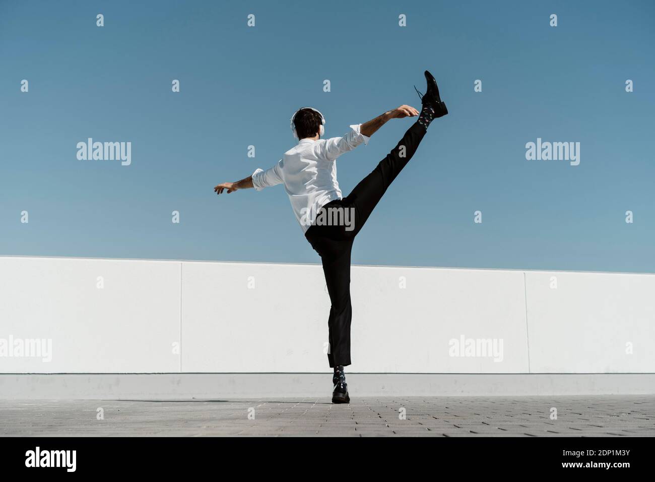 Back view of ballet dancer with headphones practising on roof terrace ...