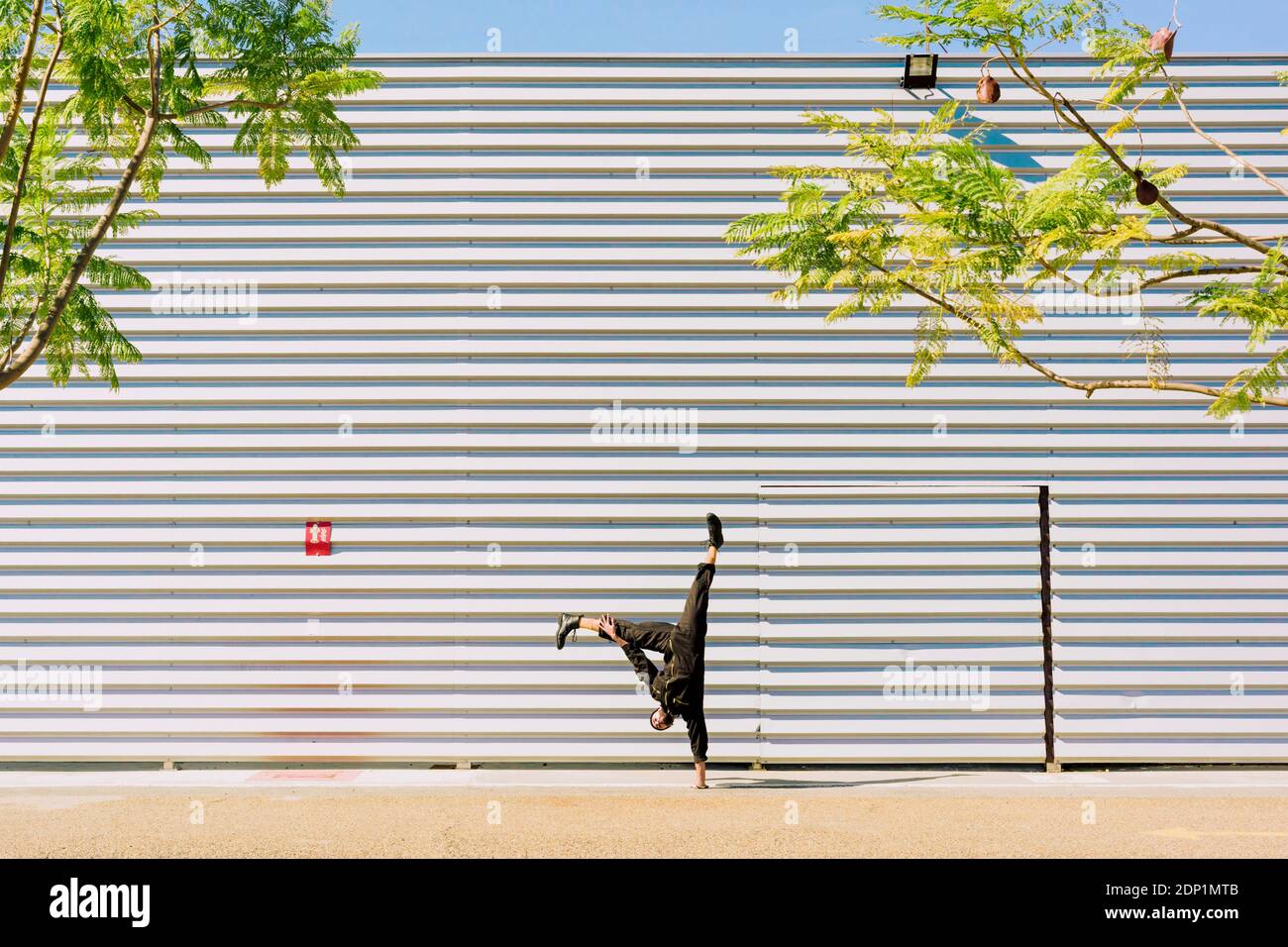 Man wearing black overall doing handstand in front of industrial ...