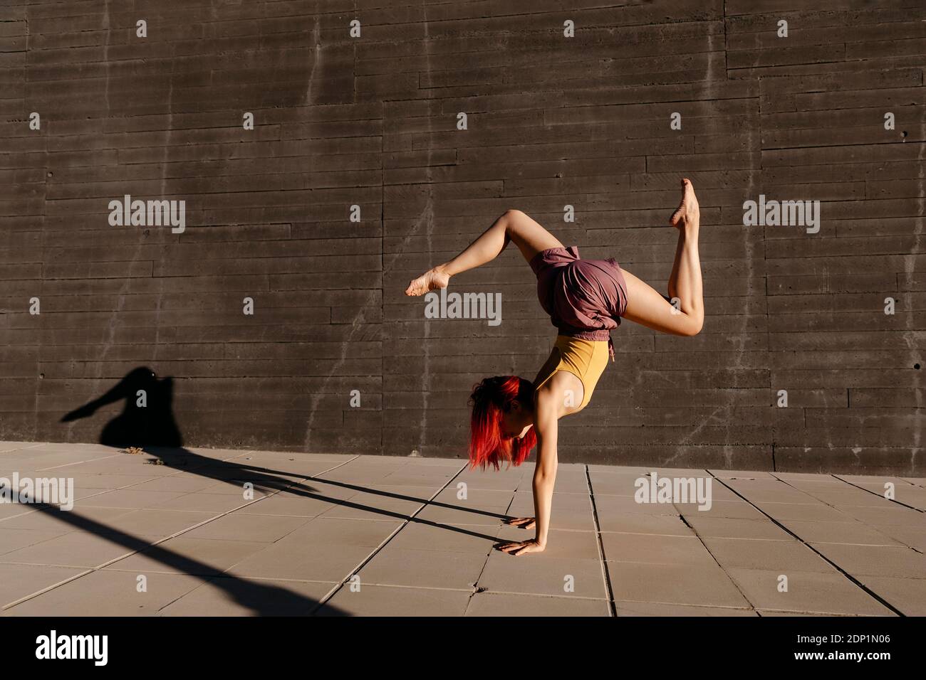 Woman doing a handstand barefoot with black urban wall background in ...