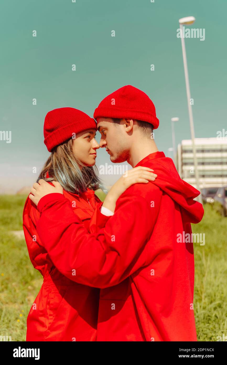 Young couple wearing red overalls and hats standing head to head ...